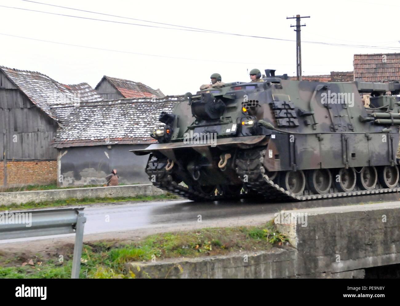 A Romanian woman watches as an M88 Hercules tank drives over a bridge ...