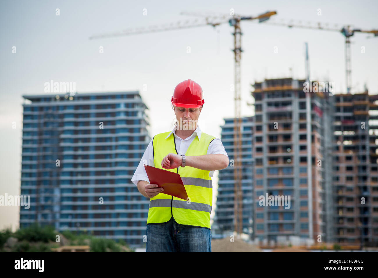 Architect on a construction site looking at his watch with buildings ...