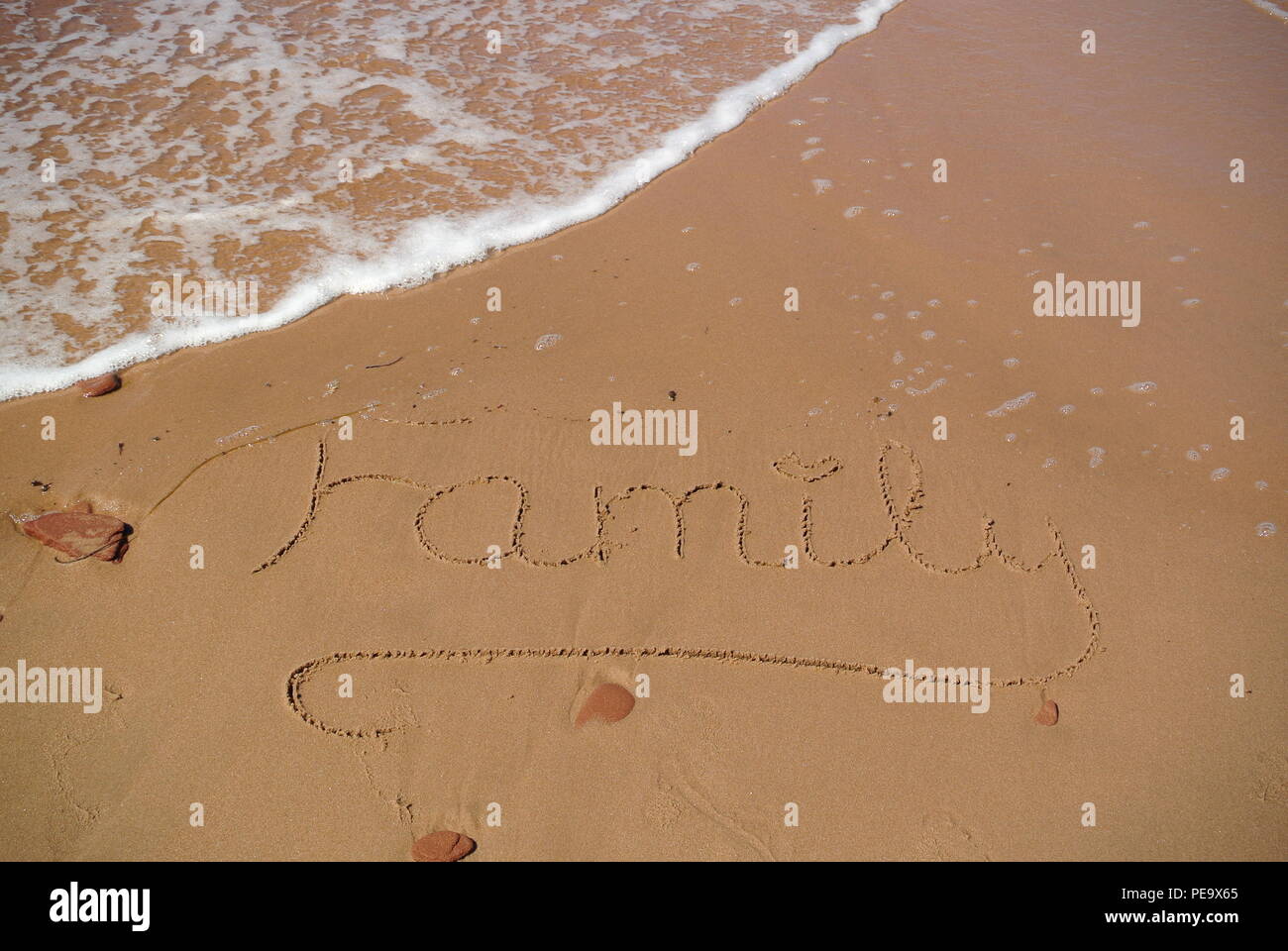 A word "Family" handwritten on the red sand on a beach with a foamy ...
