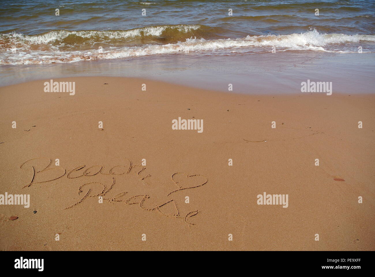Words "Beach please" beautifully handwritten on the red sand on a beach ...