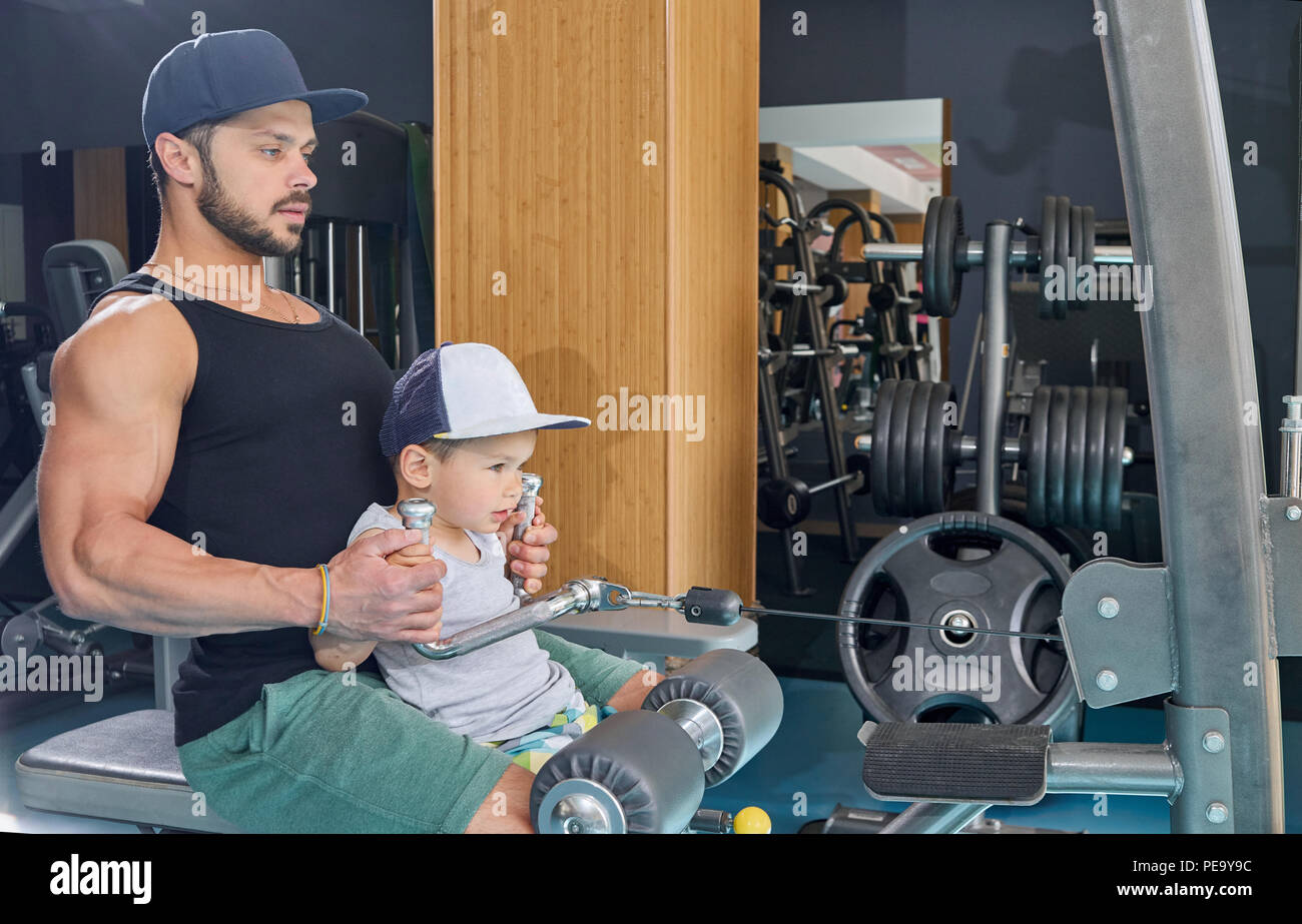 Side view of dad and little son doing arms exercises sitting on gym ...