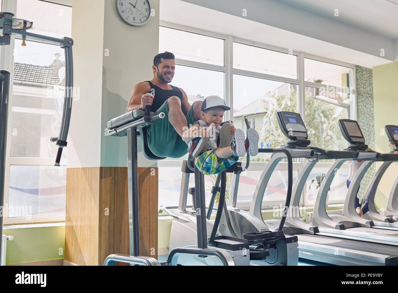 Strong father-bodybuilder doing exercises on simulator in gym keeping ...