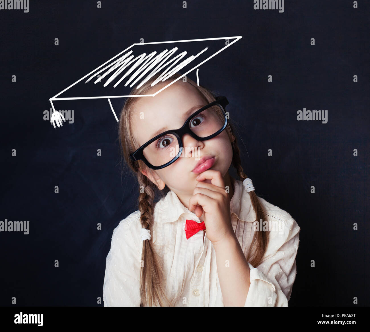 Schoolgirl in graduation hat thinking against chalkboard background in ...