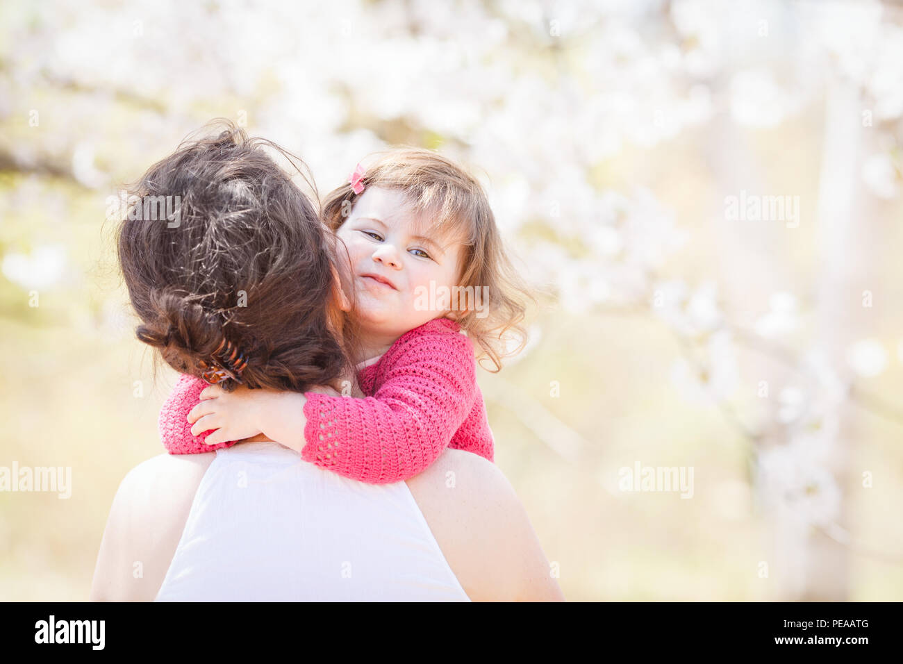 Close up portrait of caucasian mother in white dress holding hugging her daughter in pink ...