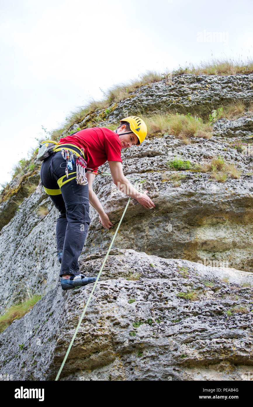 Photo from back of climbing young sports man in yellow helmet on rock ...