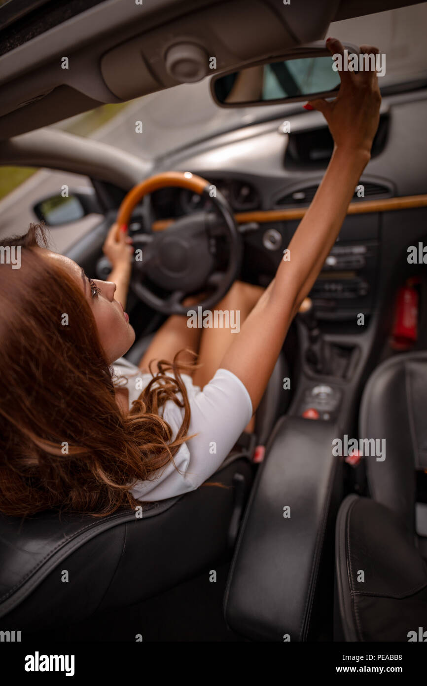 Beautiful young lady looking through the rear view mirror while driving ...