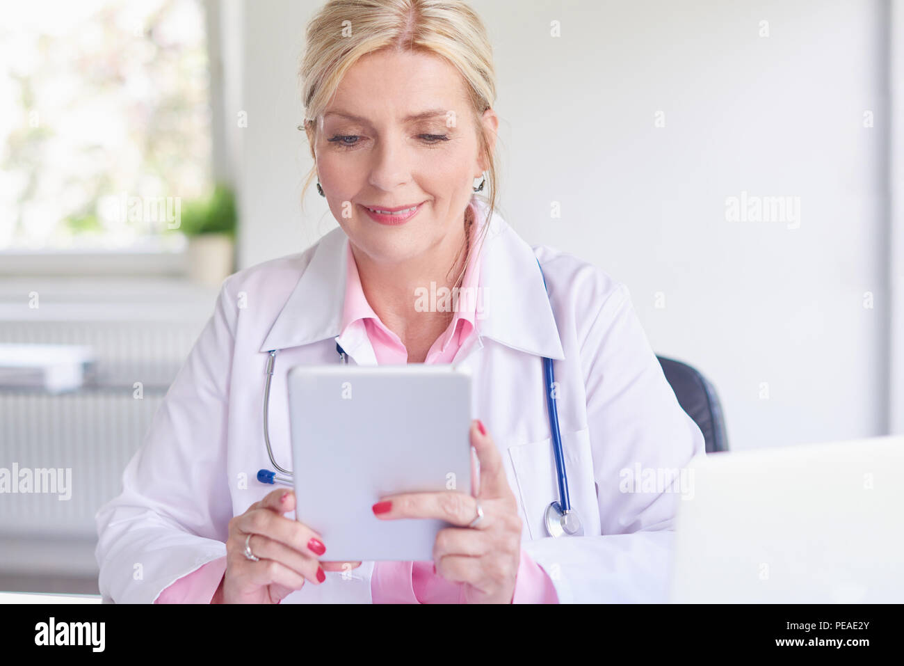 Senior female doctor using touchpad while sitting at doctor's room in ...