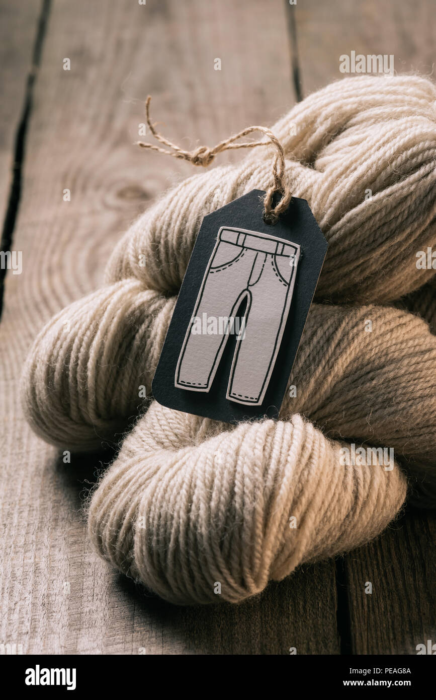 selective focus of beige yarn ball and tag with trousers on wooden ...