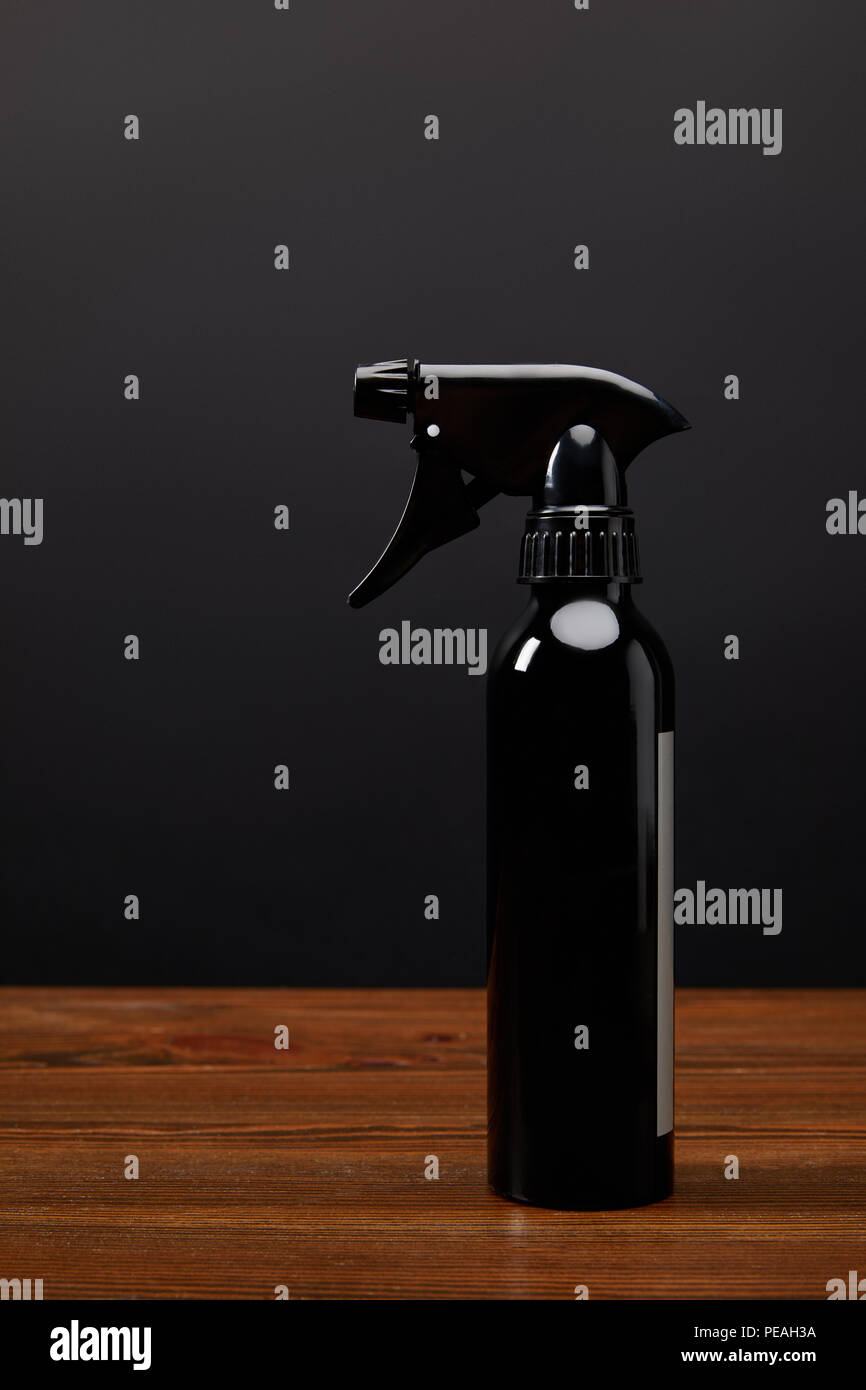 close up view of black spray bottle on wooden surface on black wall ...