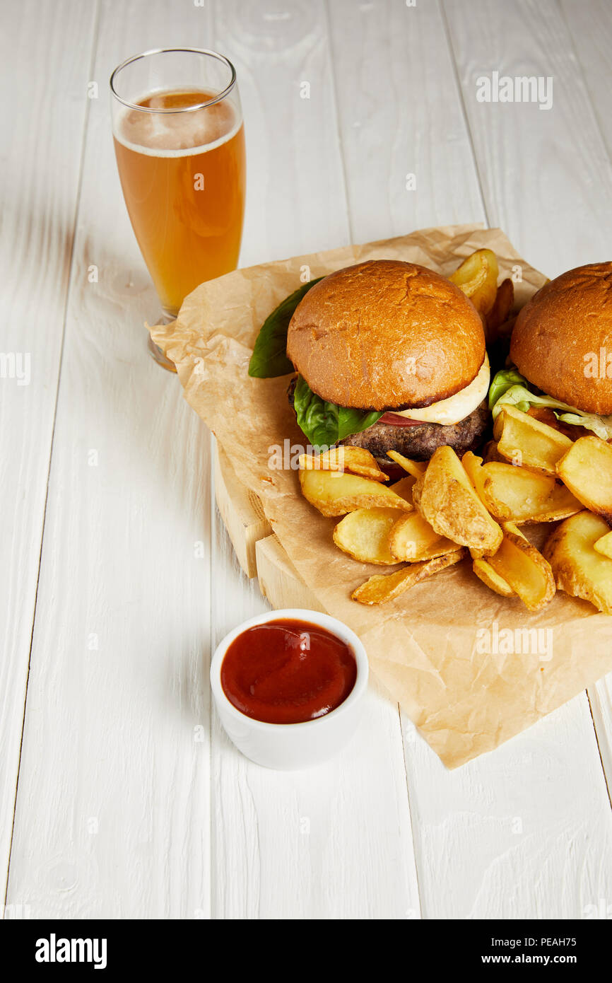 Set of junk food burgers and fries served with beer on white table ...