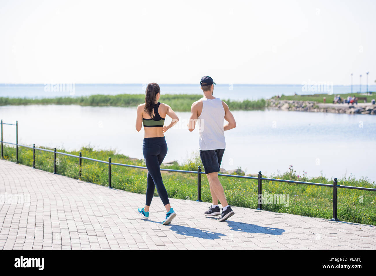 Back view portrait of active young couple running together along lake ...