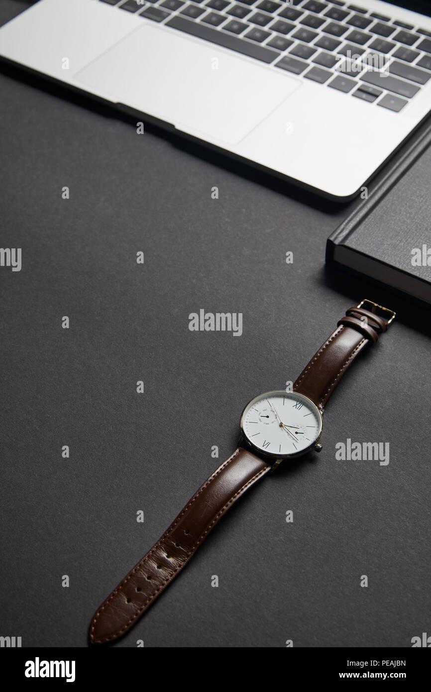 Brown watch by open laptop on black background Stock Photo - Alamy