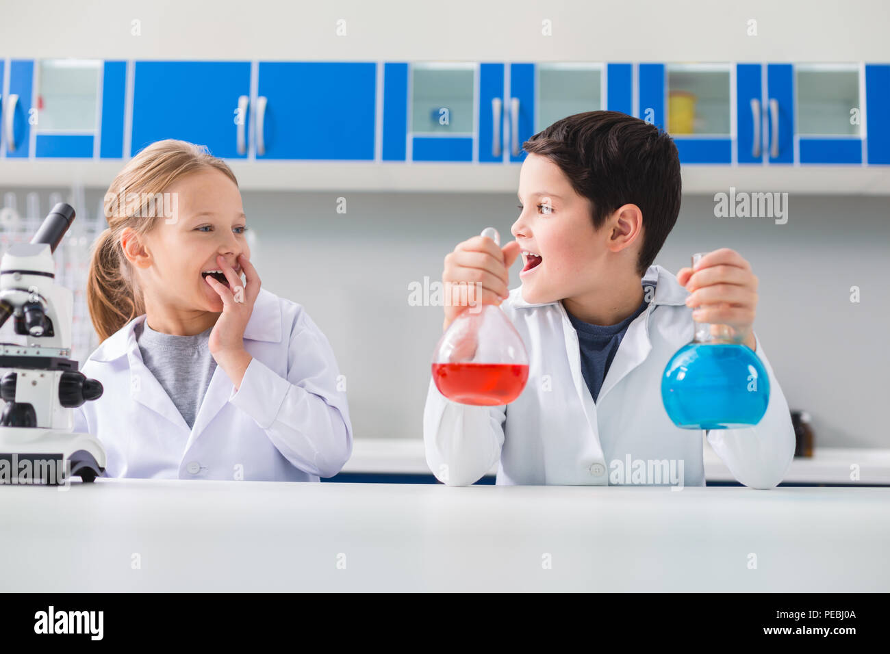 Fun in the lab. Positive happy nice boy holding flasks with reagents ...