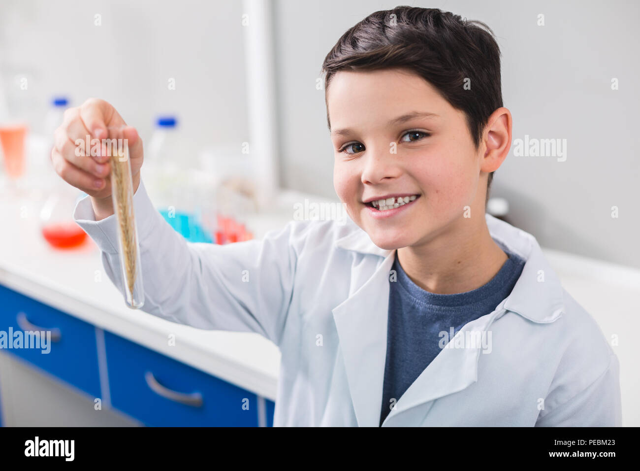 Crop in vail. Smart good looking pleased boy holding vial while staring ...
