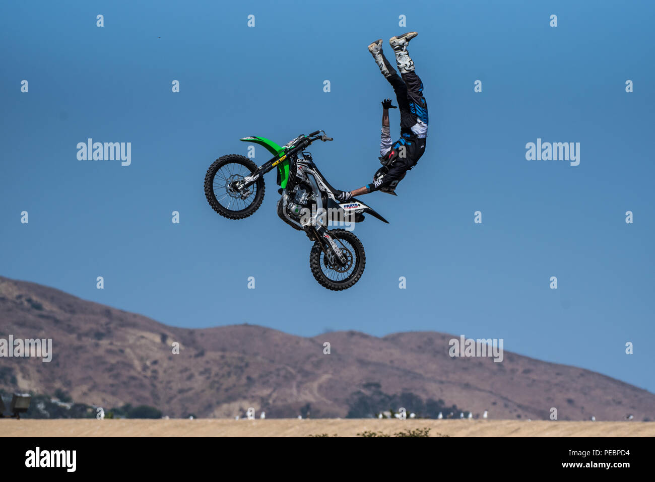 Stunt rider in black costume performs tail grab handstand on jump ...