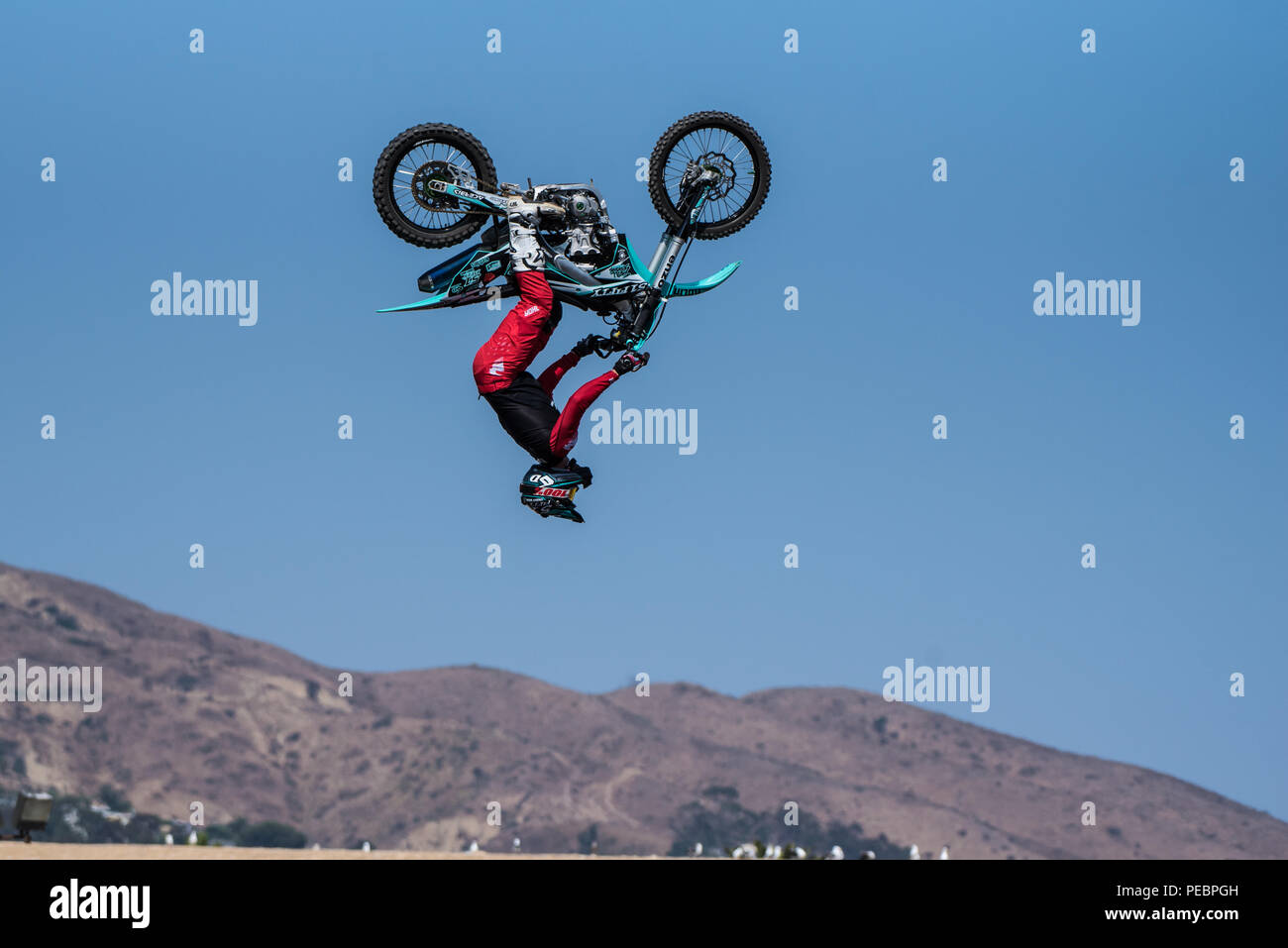 Stunt rider in red costume upside down during apex of backflip on jump ...