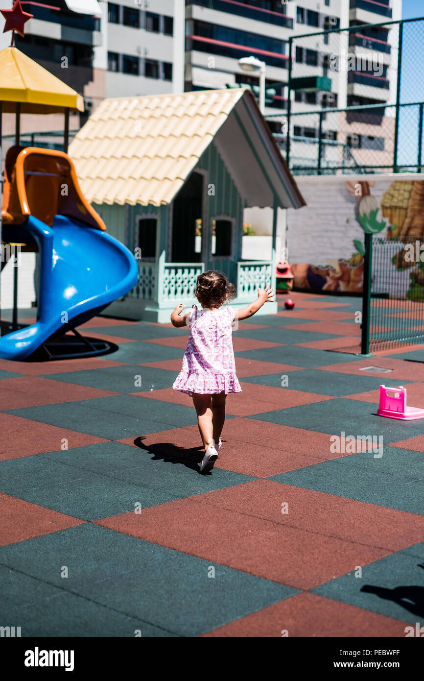 little toddler girl in pink dress running around playground, with her ...