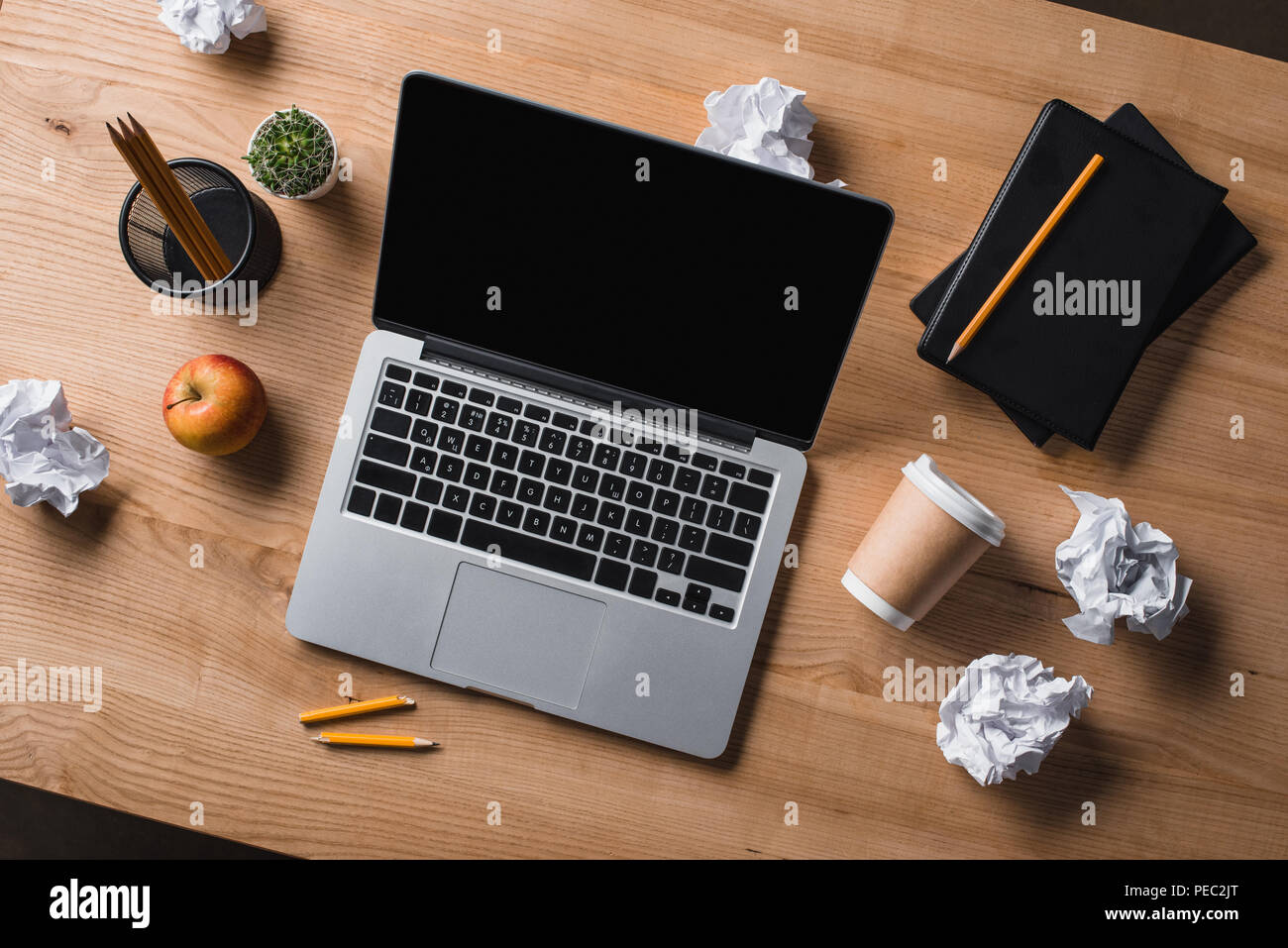 top view of messy workplace with laptop, coffee to go and crumpled ...