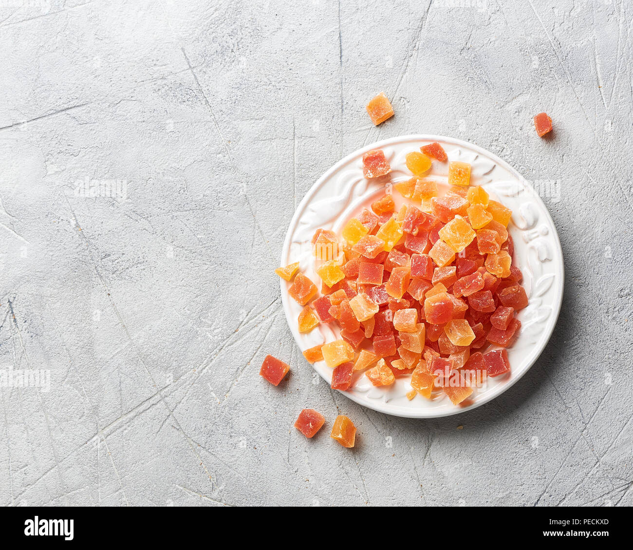 Cubes of dried apricot, mango and papaya on white plate. Candied fruits ...