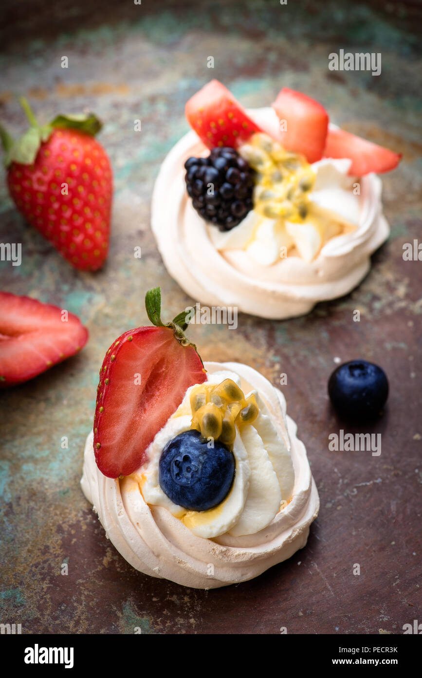 Mini Pavlova meringue cakes with berries and passion fruits on rustic ...