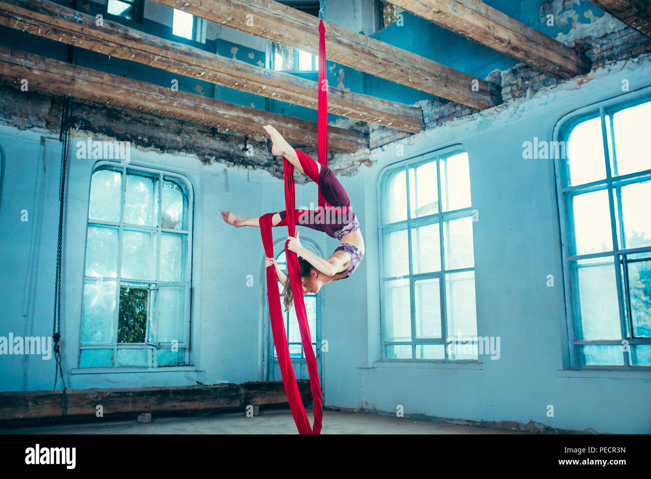 Graceful gymnast performing aerial exercise with red fabrics on blue ...