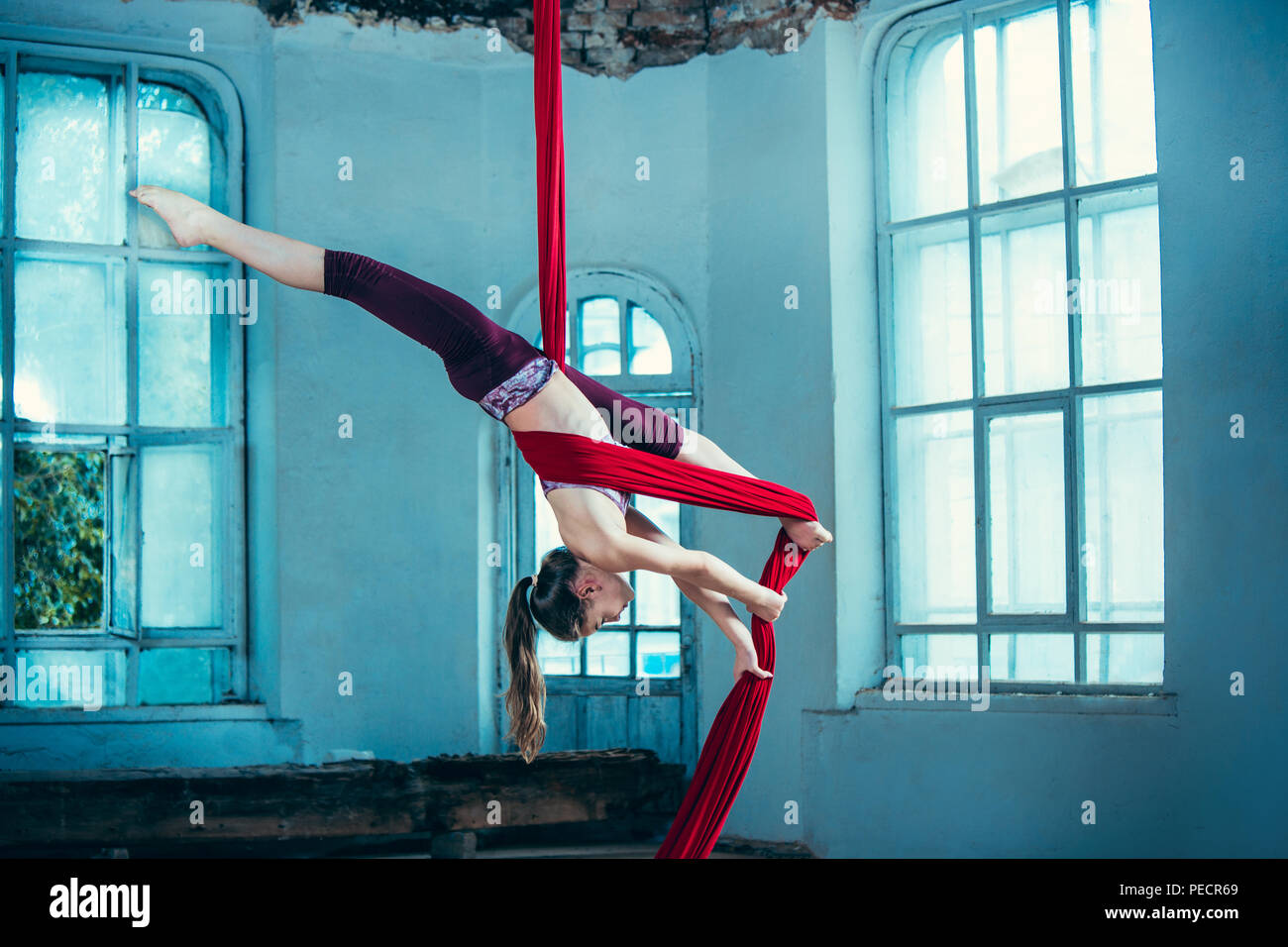 Graceful gymnast performing aerial exercise with red fabrics on blue ...