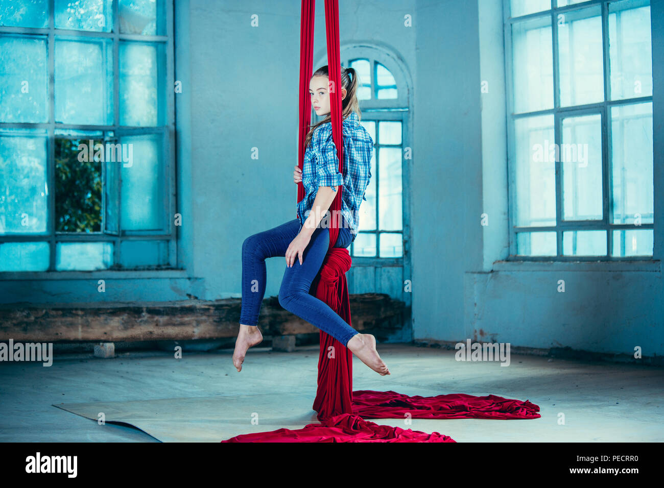 Graceful gymnast performing aerial exercise with red fabrics on blue ...