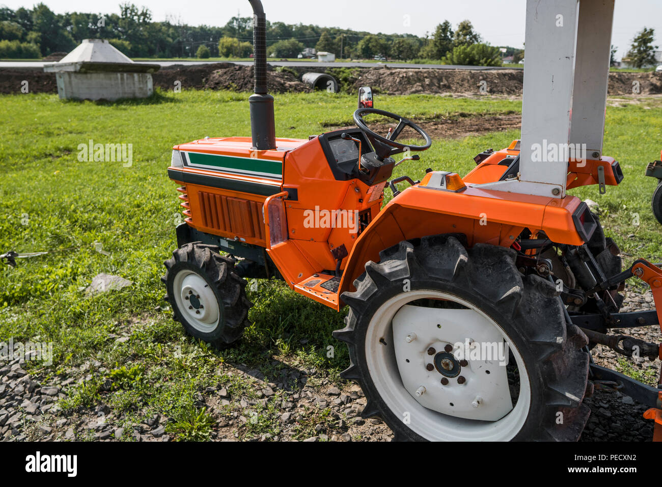 A small mini orange tractor stands on a farm yard on green grass and ...