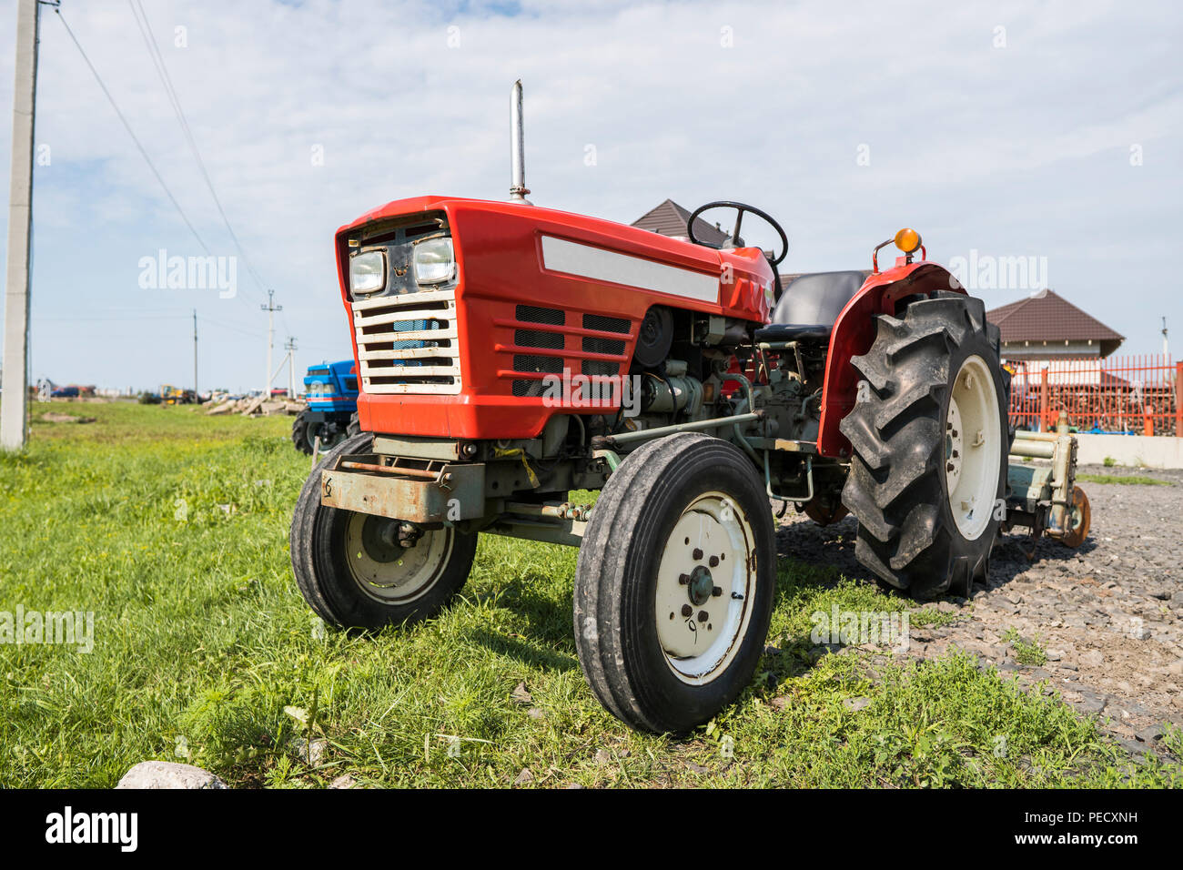 A small mini red tractor stands on a farm yard on green grass and waits ...