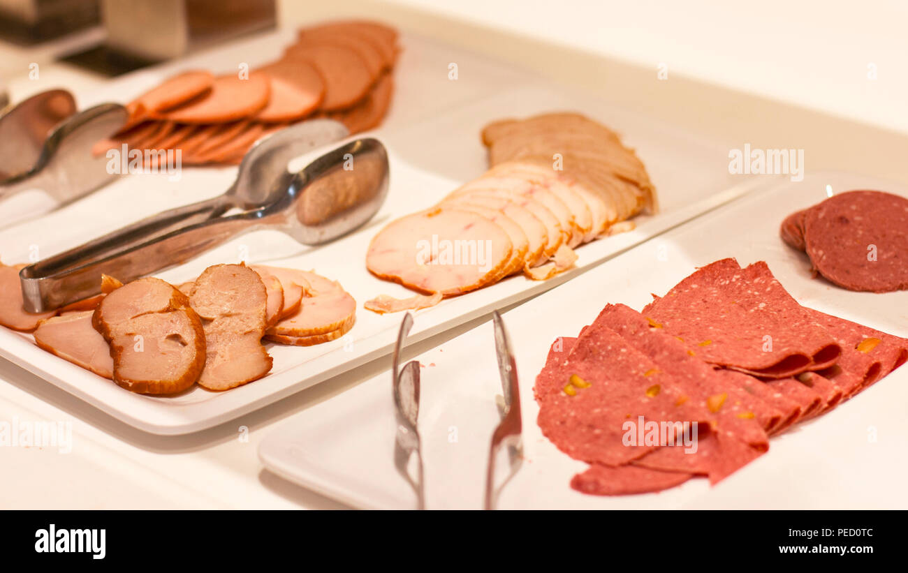 Open buffet in the hotel. Variety of ham and sausage on white plates ...