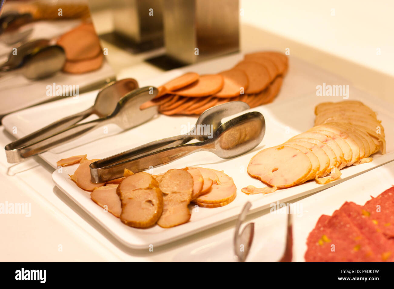 Open buffet in the hotel. Variety of ham and sausage on white plates ...