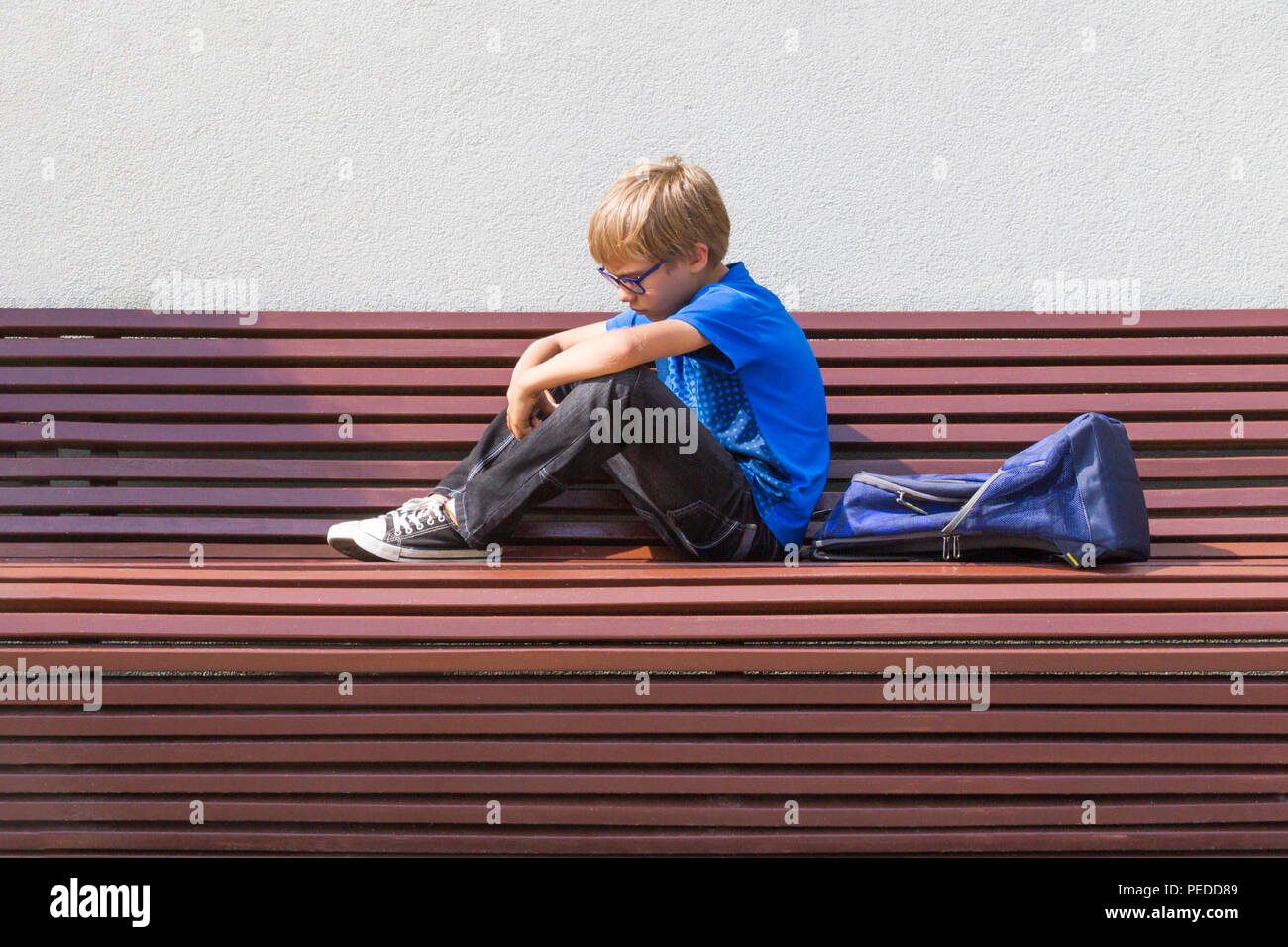Sad, tired child sitting alone on the bench outdoors Stock Photo - Alamy