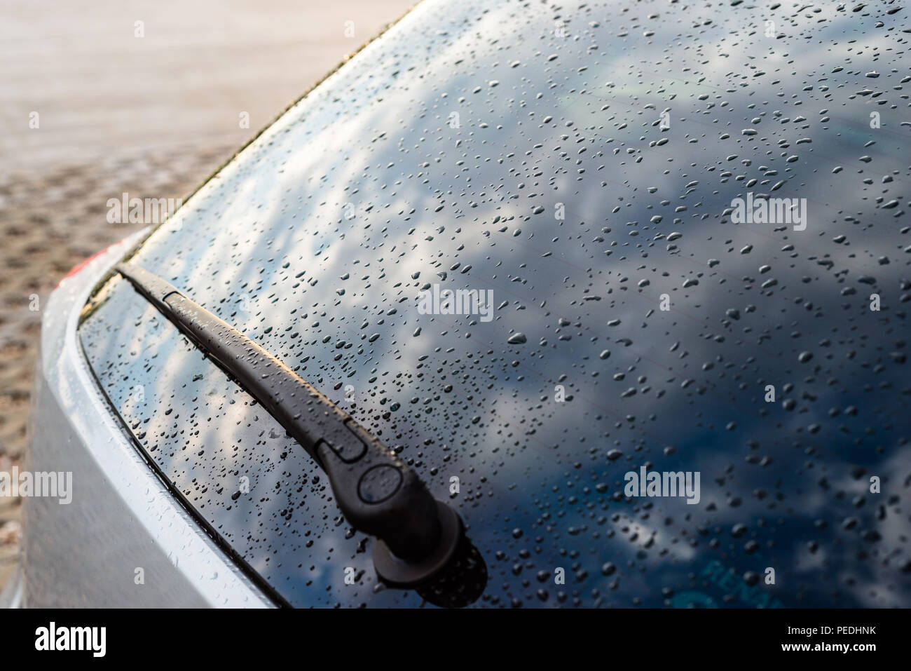 Raindrops on a silver car on the rear black window of the car with ...