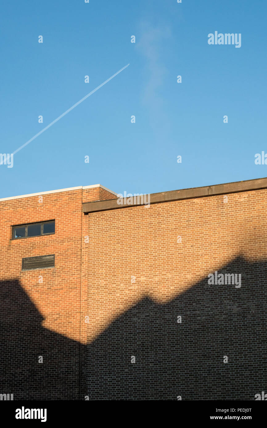 The shadow of one building on the side of another, with an aircraft con ...