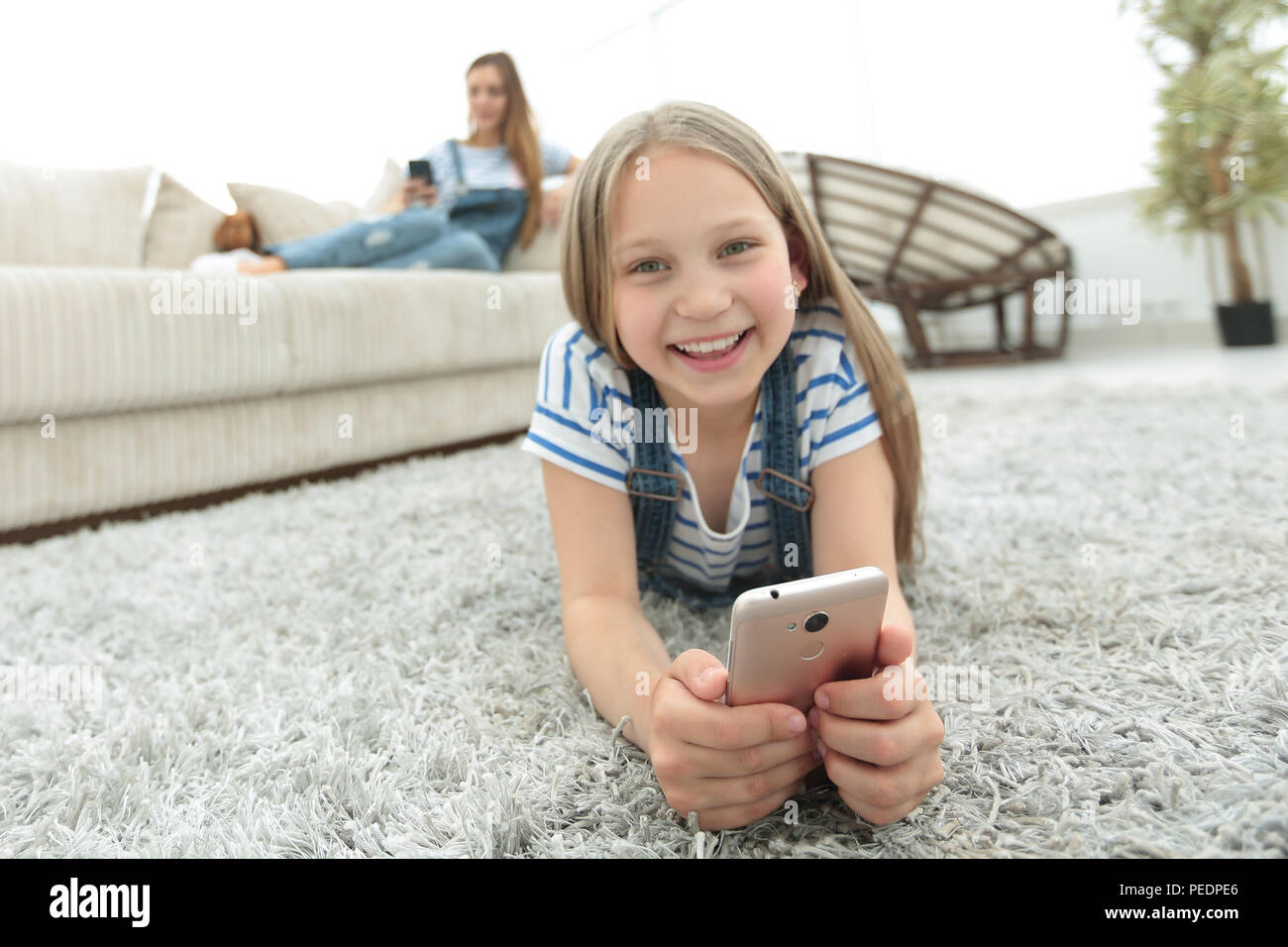 cute little girl with smartphone lying on the carpet in the living room ...