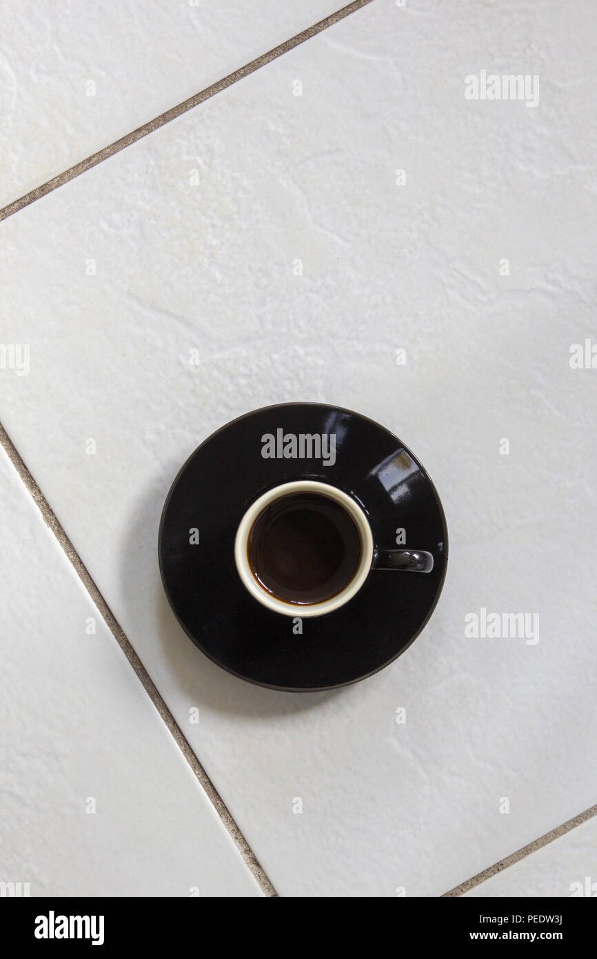 Overhead view of black espresso coffee cup on a white tiled surface ...