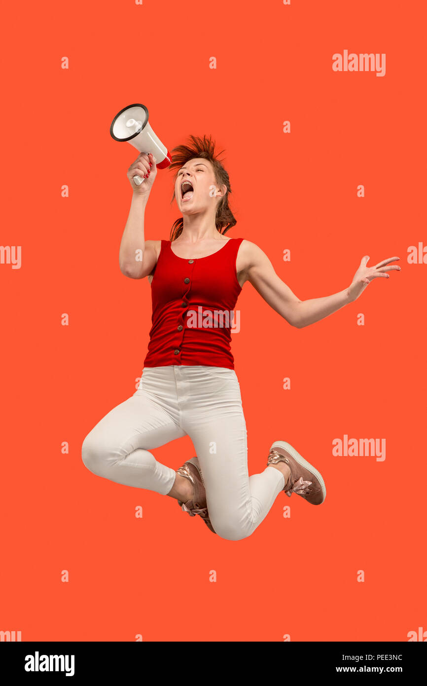 Beautiful young woman jumping with megaphone isolated over red ...