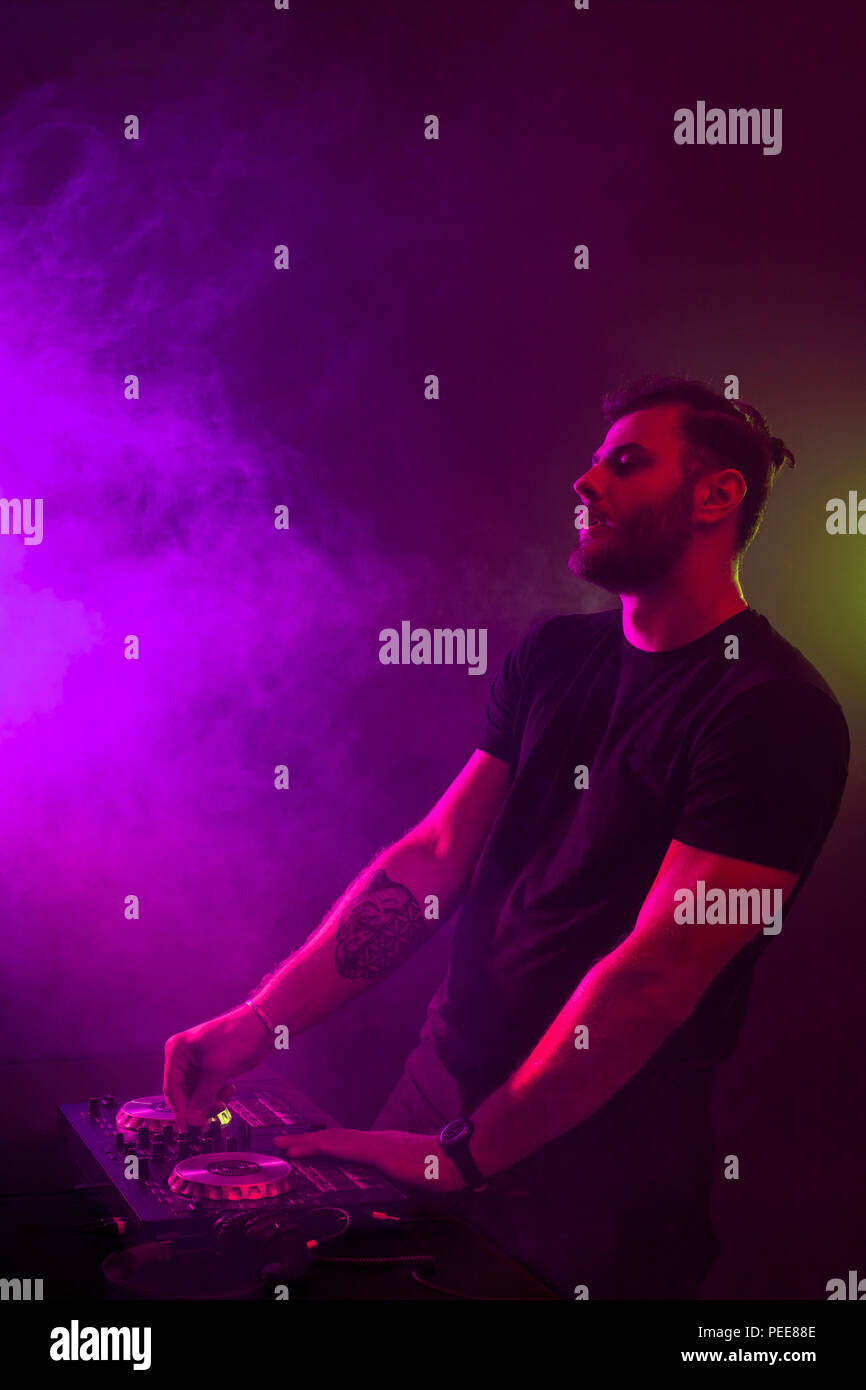 Attractive young DJ playing on turntables with color light effects ...