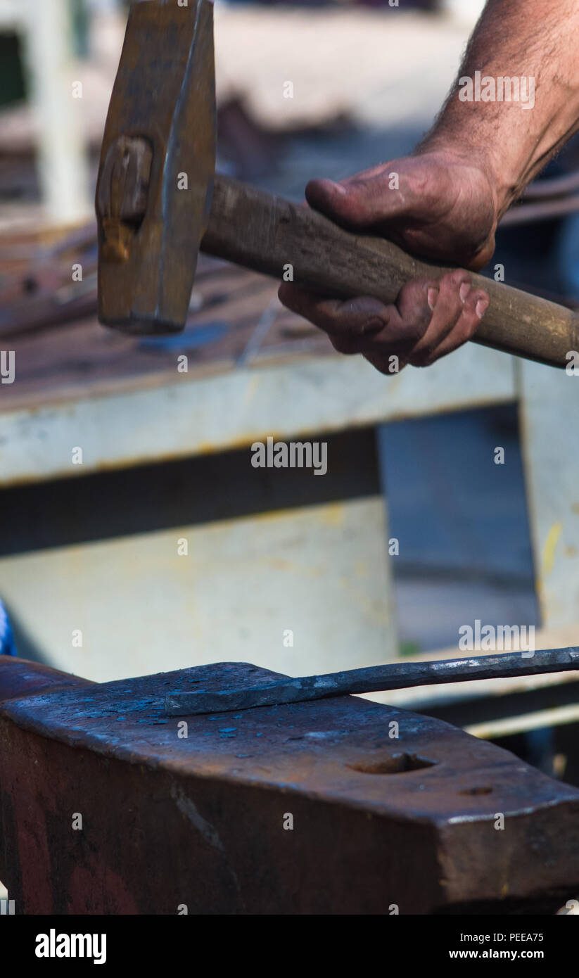 blacksmith performs the forging of hot glowing metal on the anvil ...