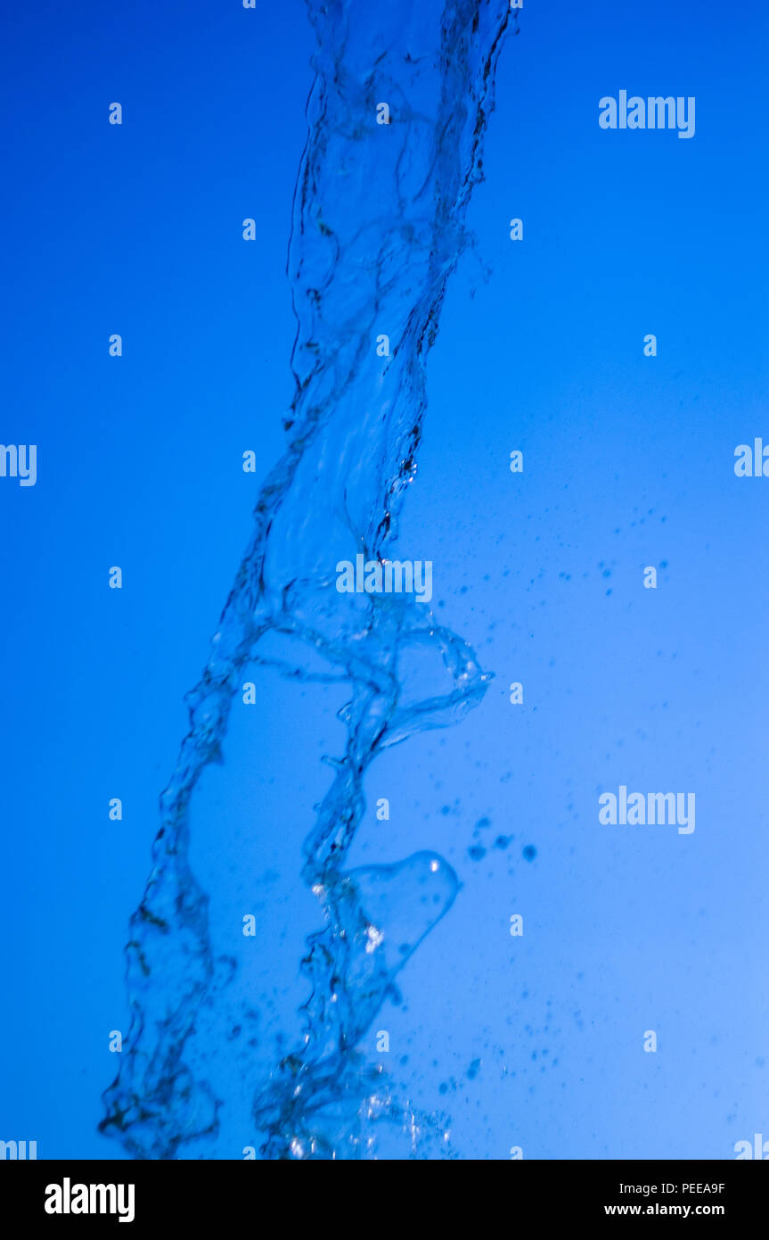 transparent falling water vertical flows against a blue sky and green ...