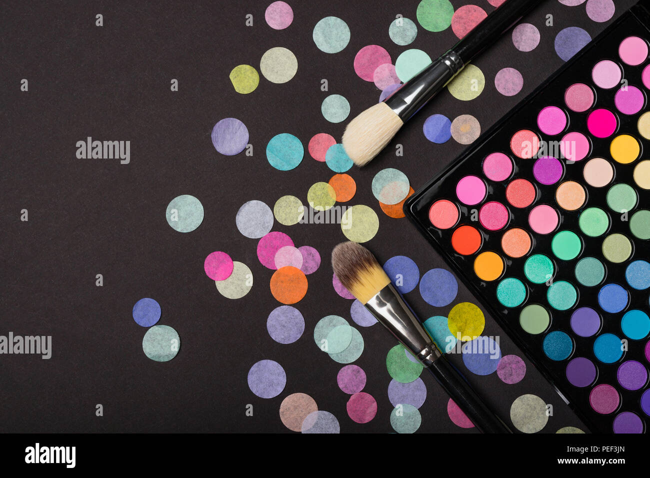 Make-up brushes with make-up palette with scattered confetti on black ...