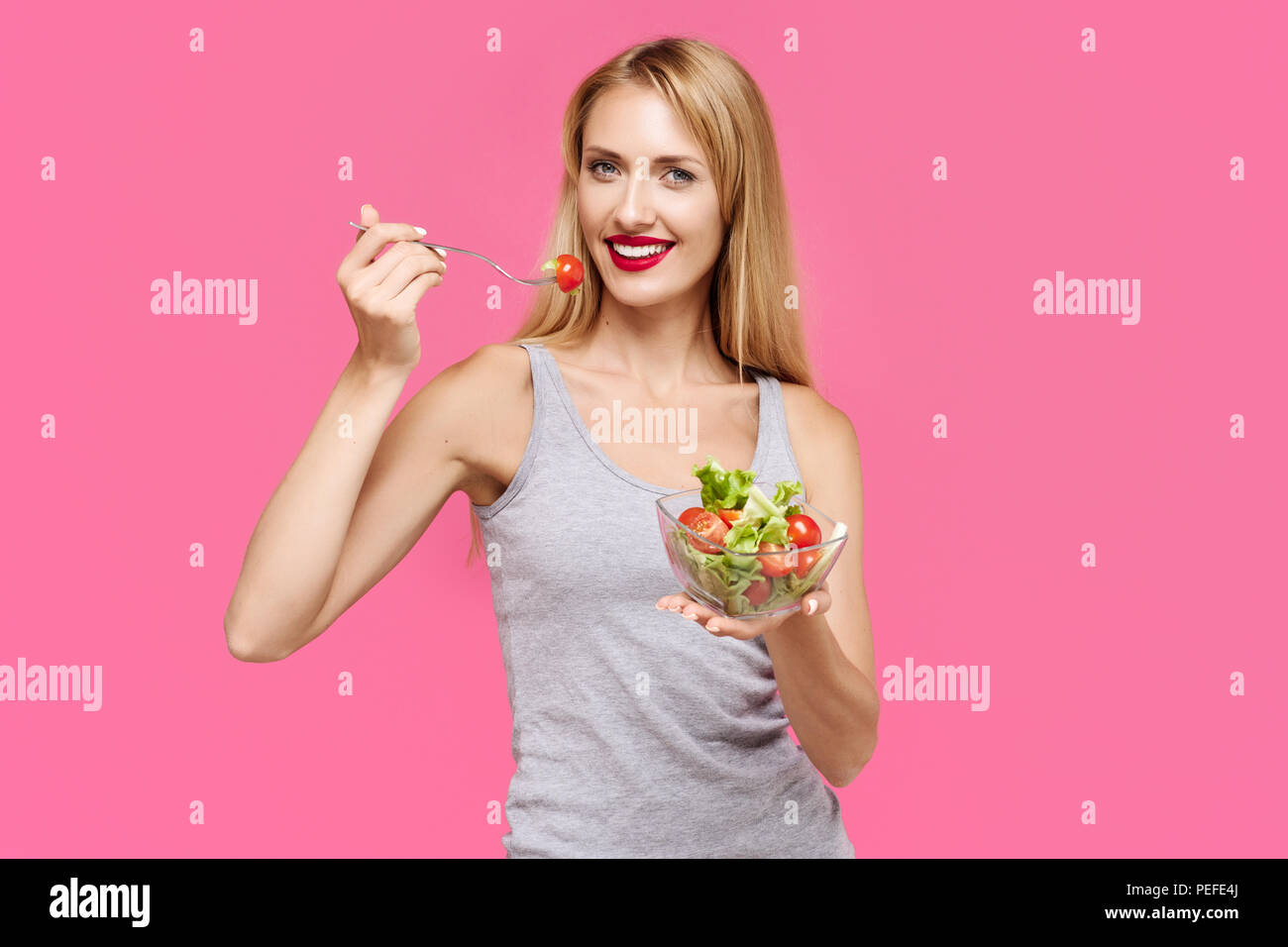 Young beautiful slender girl with a pink background eating a vegetable ...
