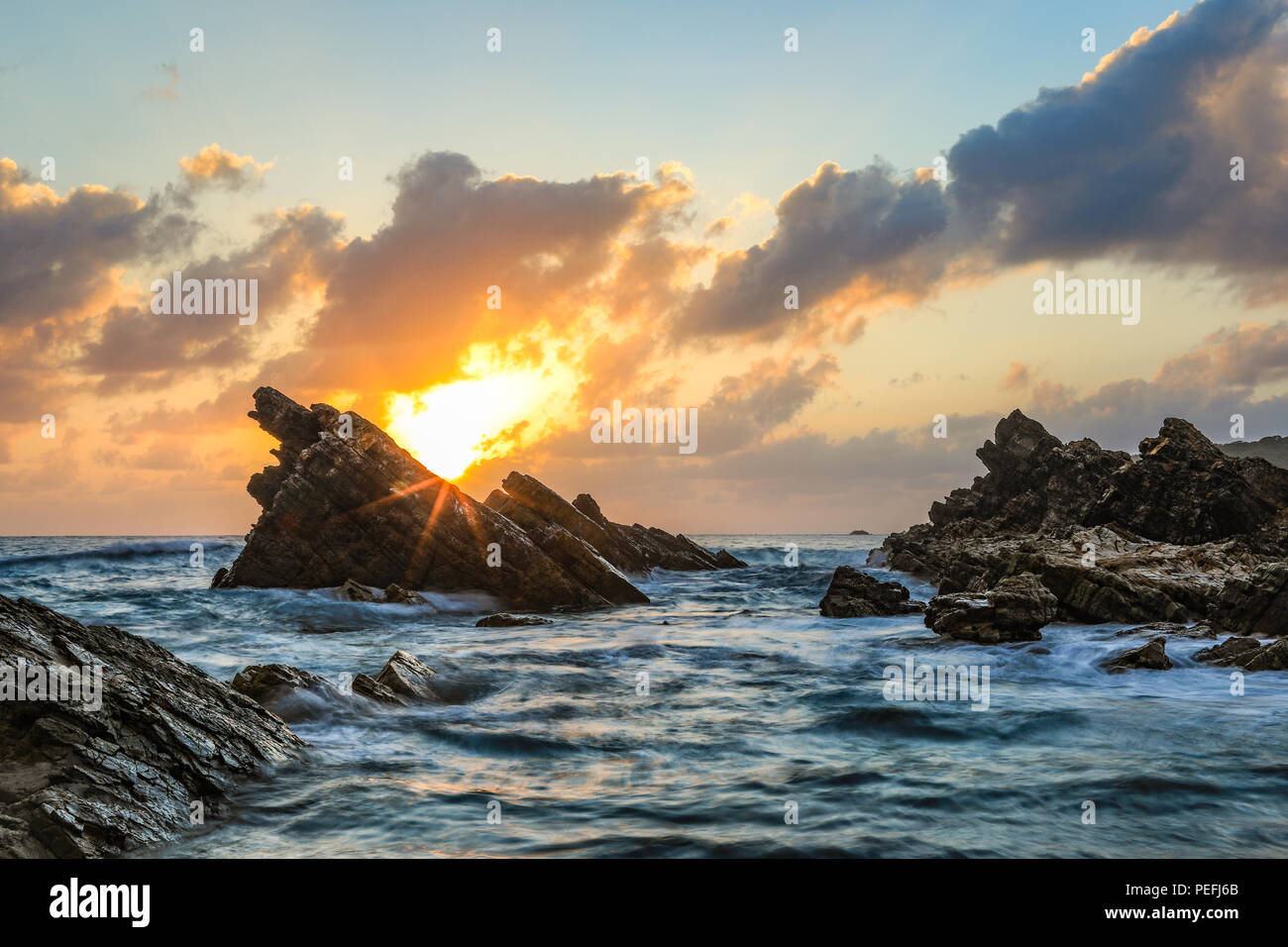 Cloudy sunrise over ocean and rocky beach Stock Photo - Alamy