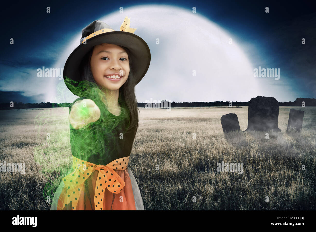 Cheerful asian witch child girl use magic wand power. Halloween concept ...