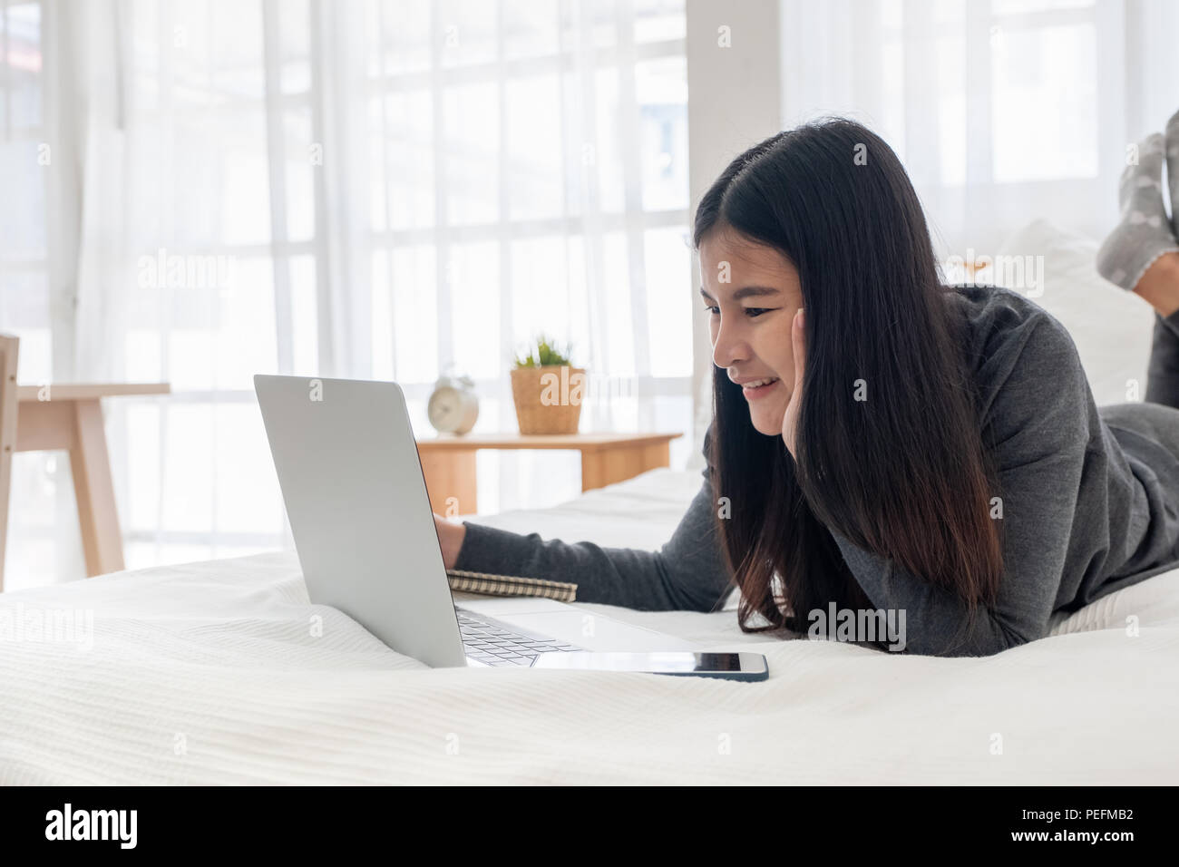 Asian woman laying on bed doing paperwork on laptop in bedroom.work at ...