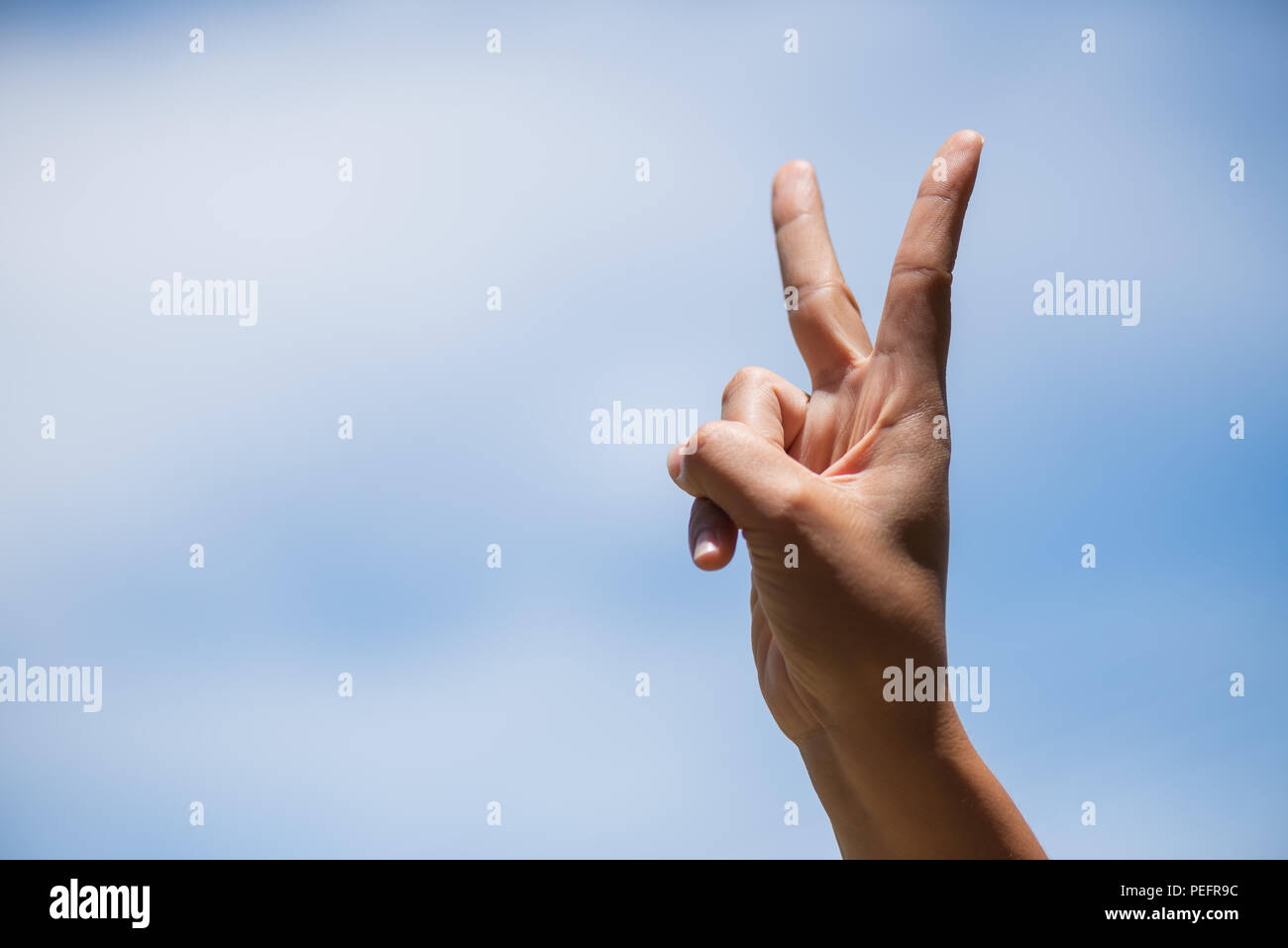 Woman hand showing two fingers as victory sign on blue sky with white ...