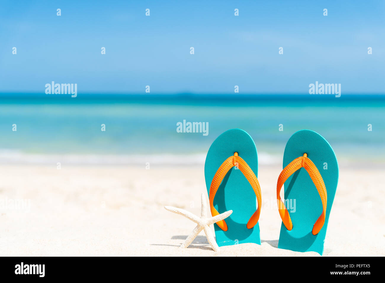 Beach accessories including flip flop, starfish and sea shell on sandy ...