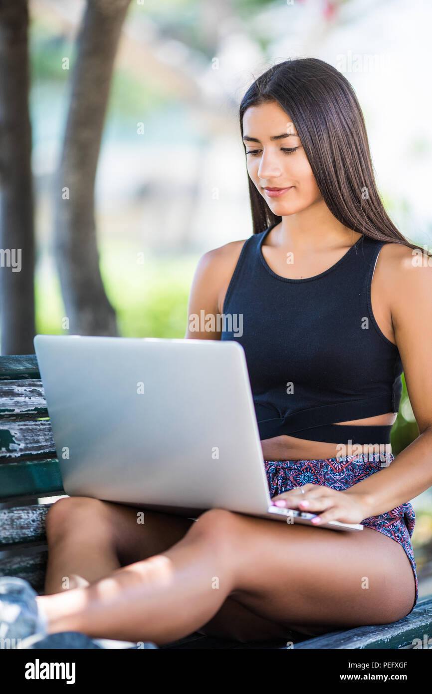 Beautiful young woman sitting in public park chatting over laptop ...