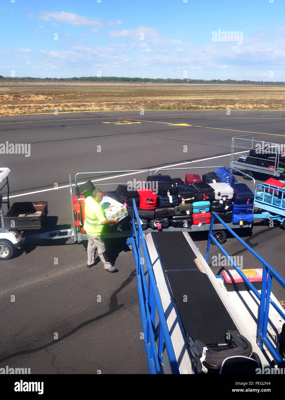 Airport handler loading baggage being put on a conveyor into a plane at ...