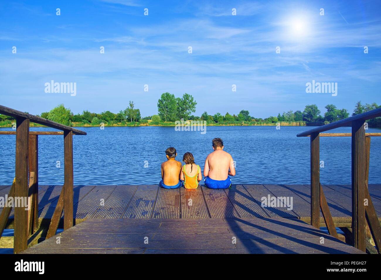 Children sitting on pier. Three children of different age - teenager ...